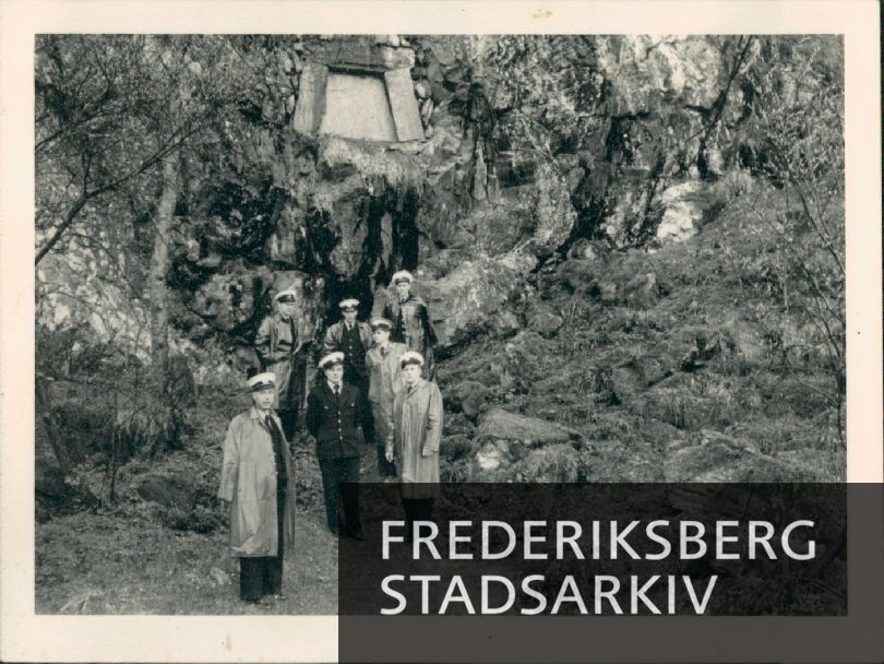 Nogle brandfolk i regnfrakker foran en forseglet skakt i klippen bagved ...